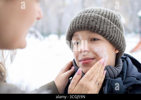 Parent caring for child applying sun protection cream on face outdoors ...