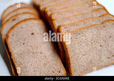 Freshly baked bread slices on cutting board against white wooden ...