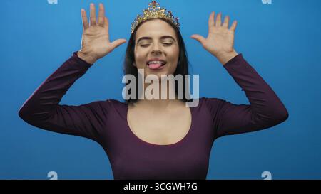 Woman wearing crown smiles against blue background showing playful ...