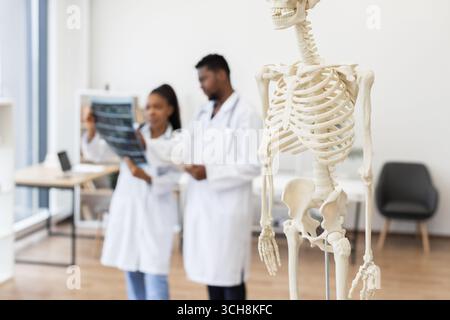 Doctors reviewing X-rays with anatomical skeleton in a bright medical ...