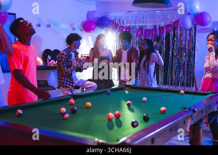 Teens celebrating birthday around pool table with balloons and festive ...