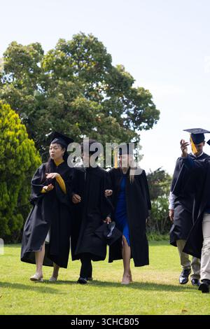 Graduating students walking outdoors in caps and gowns, smiling and ...