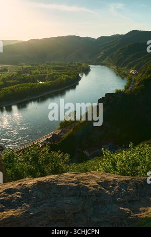 Aerial view of sun-drenched valley floor, where a narrow river meanders ...