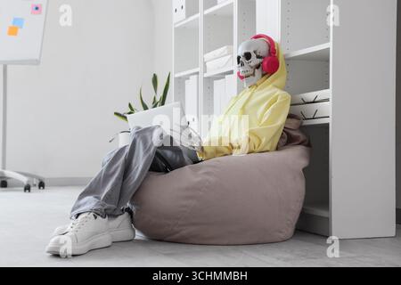 Human skeleton model with headphones and laptop on beanbag in office ...