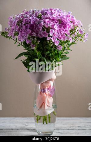 Vase with fresh blooming lilac flowers standing on table against ...