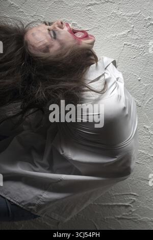 Screaming crazy woman with flying hair in straitjacket Stock Photo - Alamy