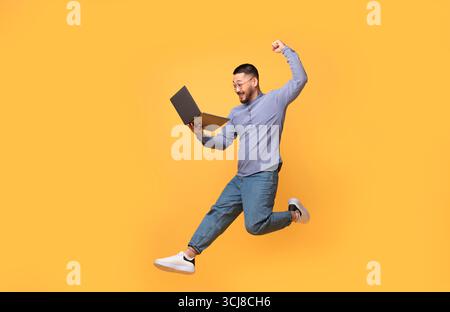 Emotional young asian man jumping up with laptop in hand Stock Photo ...