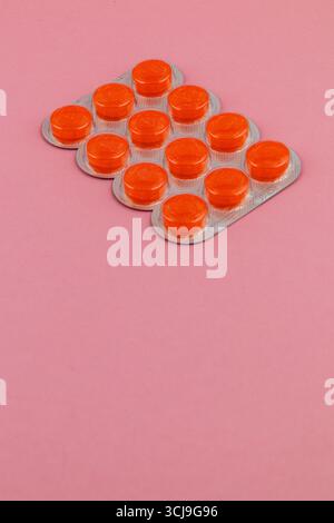 Bright orange tablets are neatly arranged in a grid pattern on a plain ...