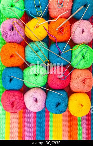 Many multi-colored balls of threads on knitted fabric on white wooden ...
