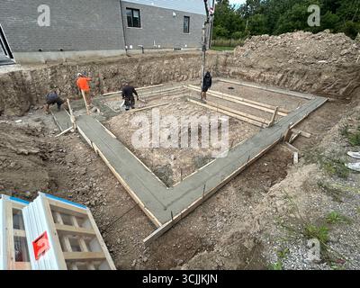 Workers pour concrete into wooden frame while using level tool to check ...