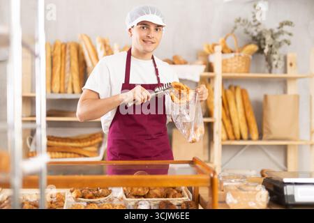 Smiling young bakery seller offering freshly baked pastries Stock Photo ...