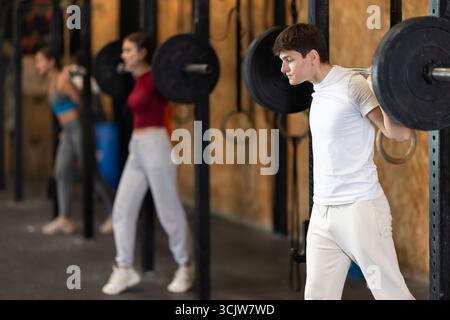 Slender guy trains muscles of arms and back using barbell and ...
