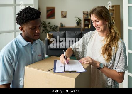 Woman Signing Delivery Form Handed by Black Man Courier Stock Photo - Alamy