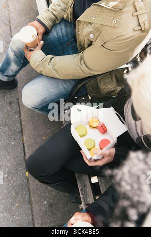 Happy couple enjoying pastries while sitting on a park bench outdoors ...