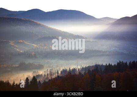 Misty mountain slope with sunlight breaking through clouds against a ...
