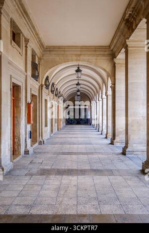 A covered stone colonnade with repeating arches stretches through the ...
