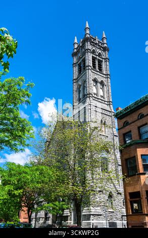 A historic stone church tower rises above terracotta rooftops with ...