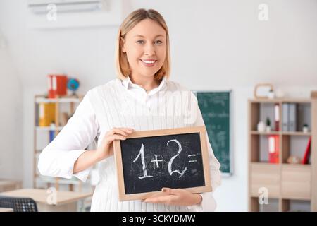 Mature female math teacher with small blackboard in classroom Stock ...