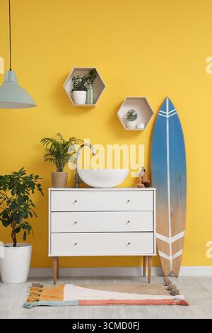 Surfboard, table and houseplants near yellow wall Stock Photo - Alamy