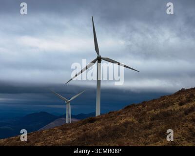 Two wind turbines stand silhouetted against a vibrant orange sunset sky ...