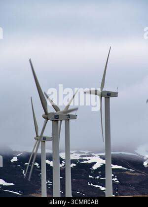 Two wind turbines stand silhouetted against a vibrant orange sunset sky ...