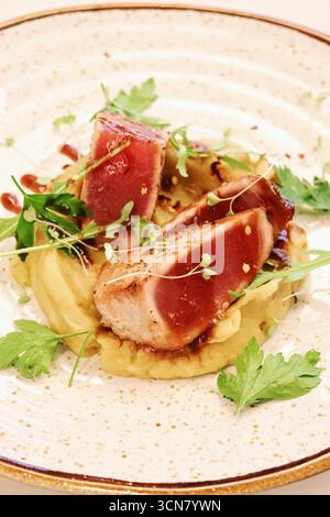 Seared tuna steak served on white plate. Raw red center shows rare ...