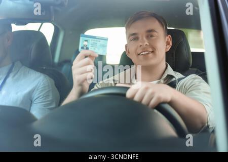 Young man with instructor after passing driving license test outdoors ...