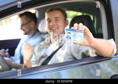 Young man with instructor after passing driving license test outdoors ...