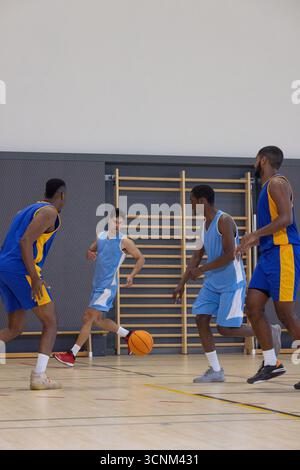 Diverse male basketball players defending and passing ball on court in ...