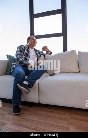 Asian man resting on couch using smartphone while sick at home Stock ...