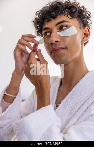 Young hispanic man wearing beauty face mask and bath robe in hurry ...