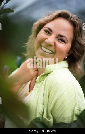 A joyful woman enjoys a serene moment amidst dense greenery, bathed in ...