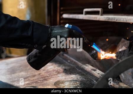A chef using a gas blowtorch to flame-grill beef cube steaks on a wire ...