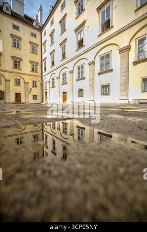 A puddle in the courtyard of the Hofburg Palace perfectly mirrors the ...