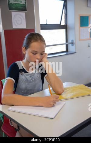 preteen girl writing in notebook while learning near laptop in living ...