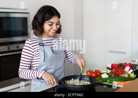 Beautiful woman frying rice with vegetables in kitchen Stock Photo - Alamy