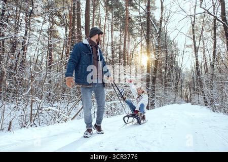 Bearded young man pulling sled with his wife sitting on it Stock Photo ...