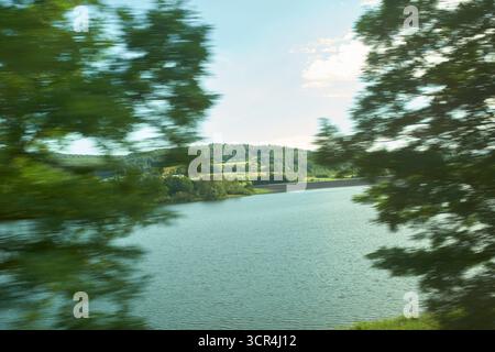 A scenic view of a lake surrounded by greenery and mountains on a sunny ...