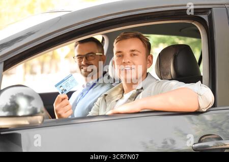 Young man with instructor after passing driving license test outdoors ...