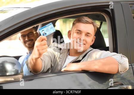 Young man with instructor after passing driving license test outdoors ...
