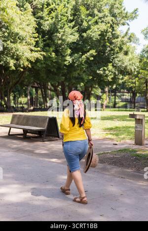 A woman walks through the park, carrying her coat over her arm on June ...