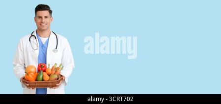 Male doctor holding basket with vegetables and vitamins on white ...