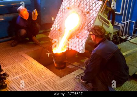 Manual workers pouring molten bronze in container at foundry Stock ...