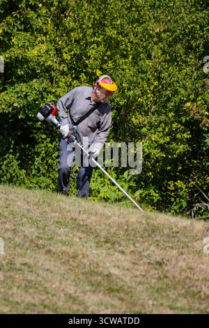 Man mowing tall grass with string trimmer in field, landscape ...