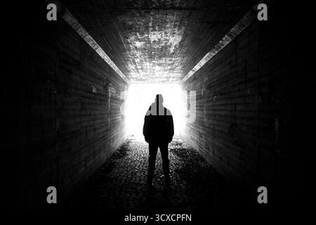 Sinister scene of man in silhouette in dark tunnel looking towards the ...