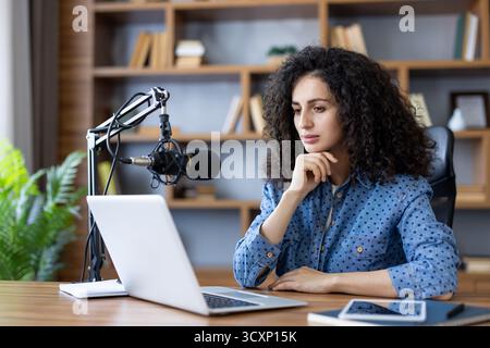 Young curly female recording podcast from home and talking into a ...