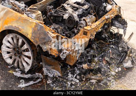 A car wreck lays abandoned by the roadside, heavily burned and charred ...