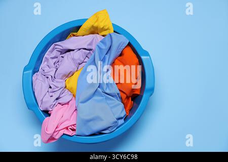 Plastic basin with clothes on light purple background, top view. Space ...