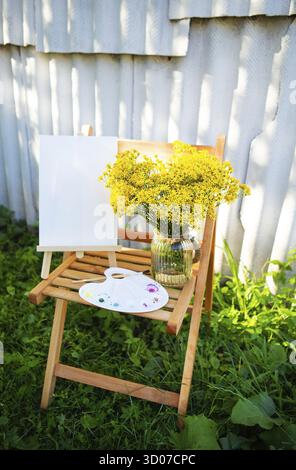 A palette of watercolor multicolored paints stands on a wooden chair ...