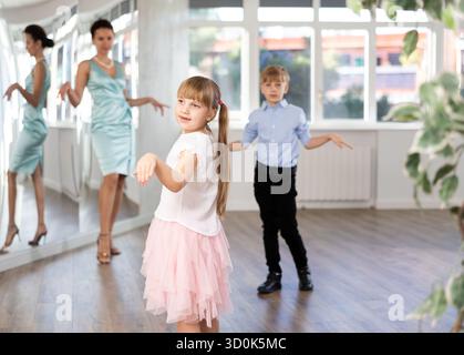 Girl rehearsing elegant curtsy with boy dance partner and female ...